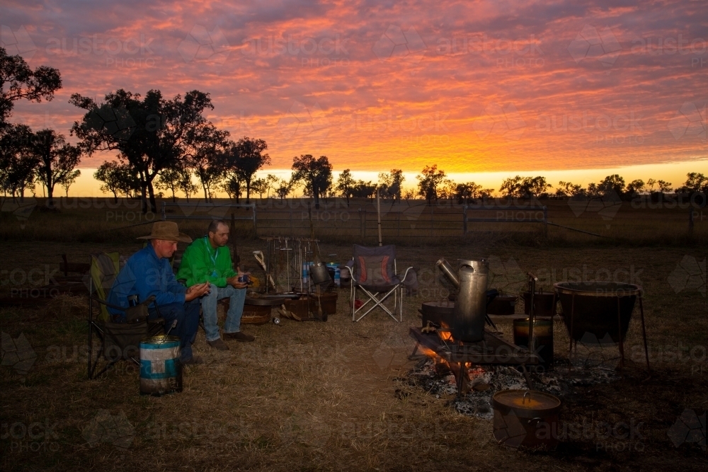 Image of Two men sitting by a campfire at sunrise. - Austockphoto