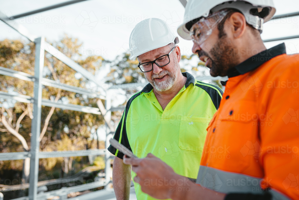 Image of Two men wearing safety gear on the work site with one holding ...