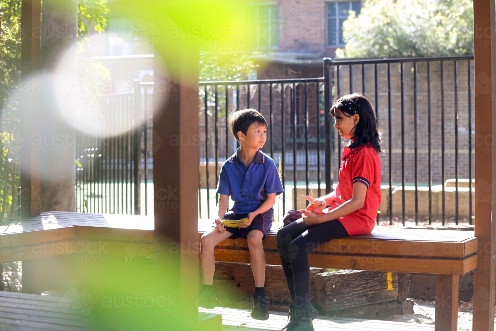 Image of Two primary school students sitting on a bench talking ...