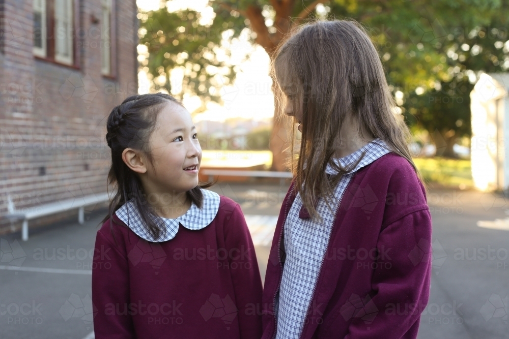 Image of Two school girls talking together in the schoolyard - Austockphoto