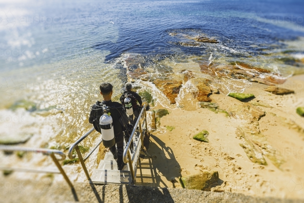 Image of Two scuba divers walking down stairs to the ocean - Austockphoto