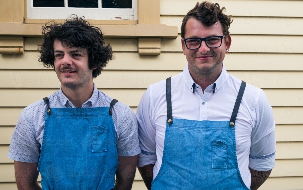 Image of Two smiling waiters wearing matching aprons - Austockphoto