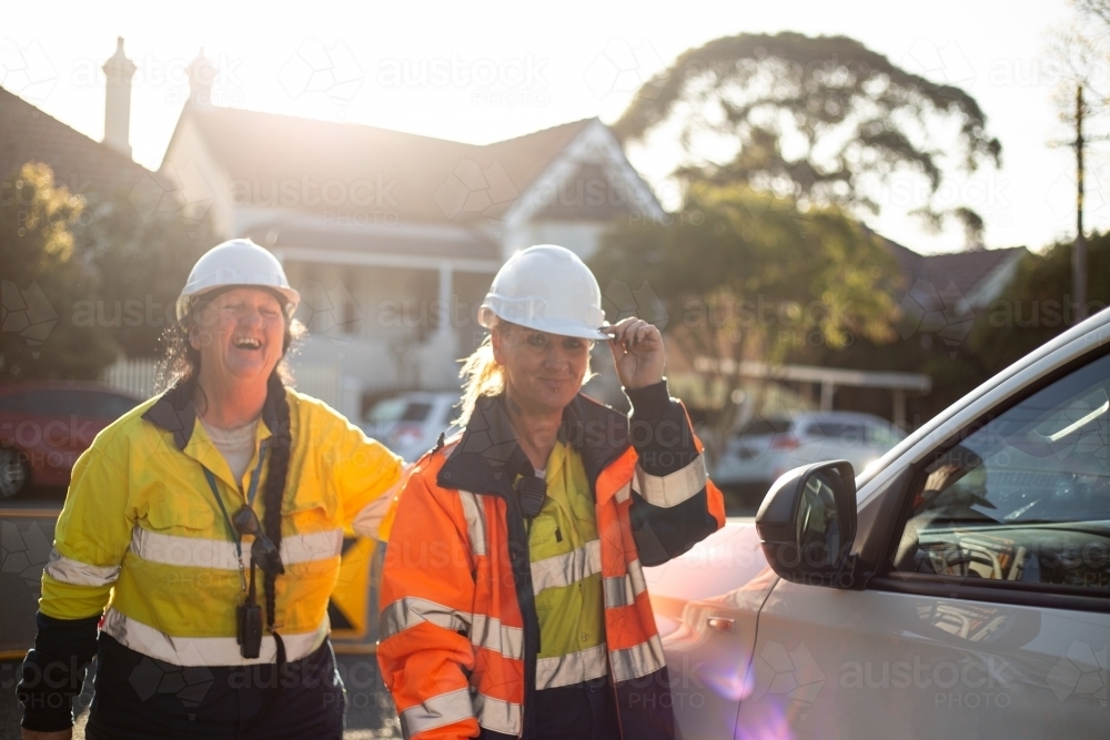 Image of Two smiling women road workers wearing white helmet on sunset ...