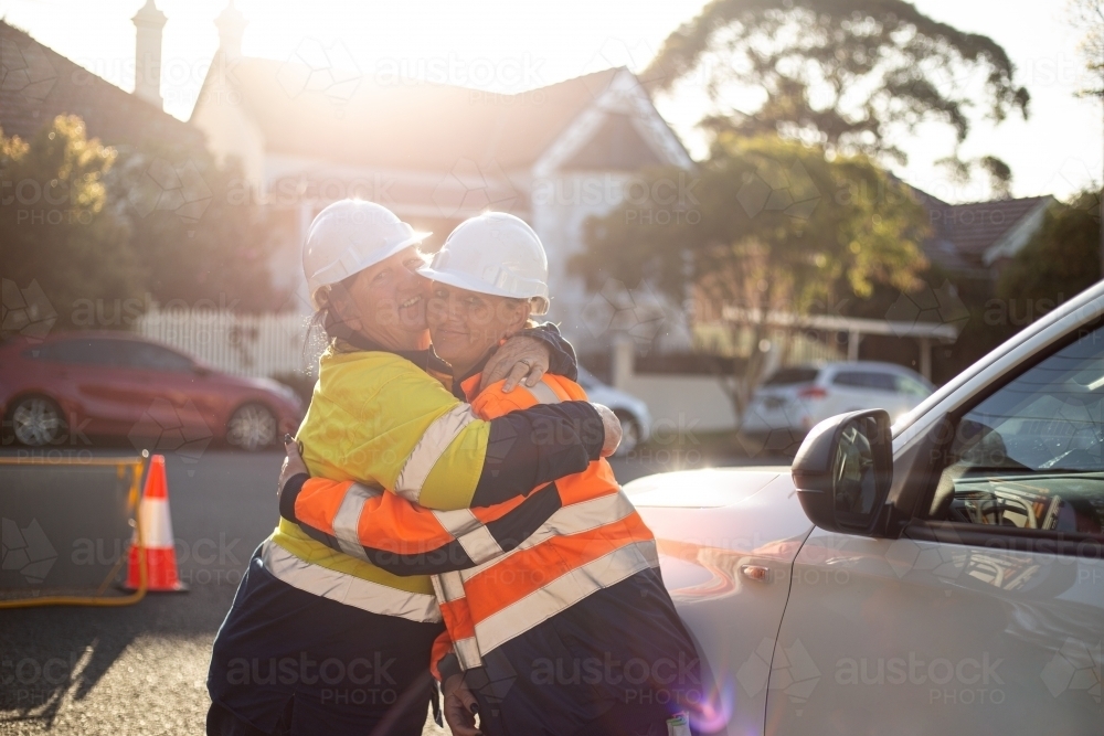 Image of Two smiling women road workers with white helmets hugging each ...