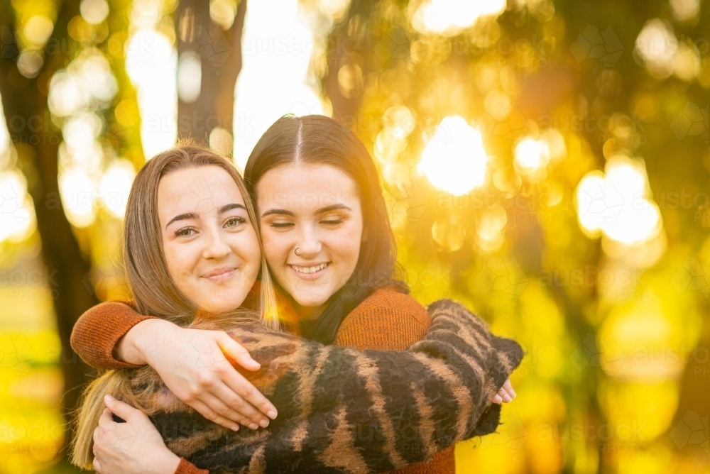 Image of two teenage girls having a big hug in golden light - Austockphoto
