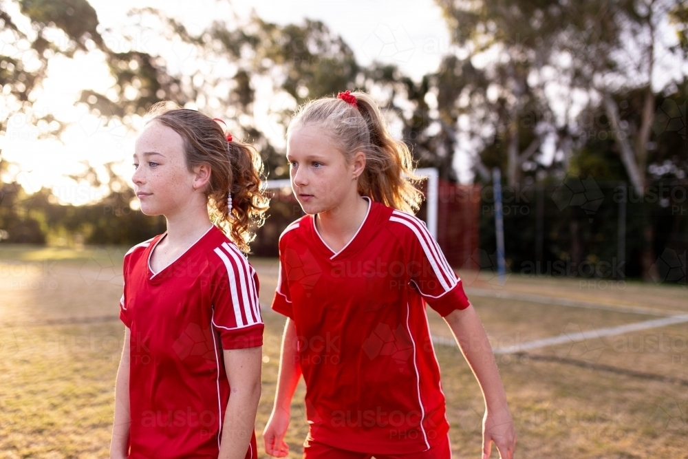 Image of Two tween girls in soccer shirts walking together on a sports ...