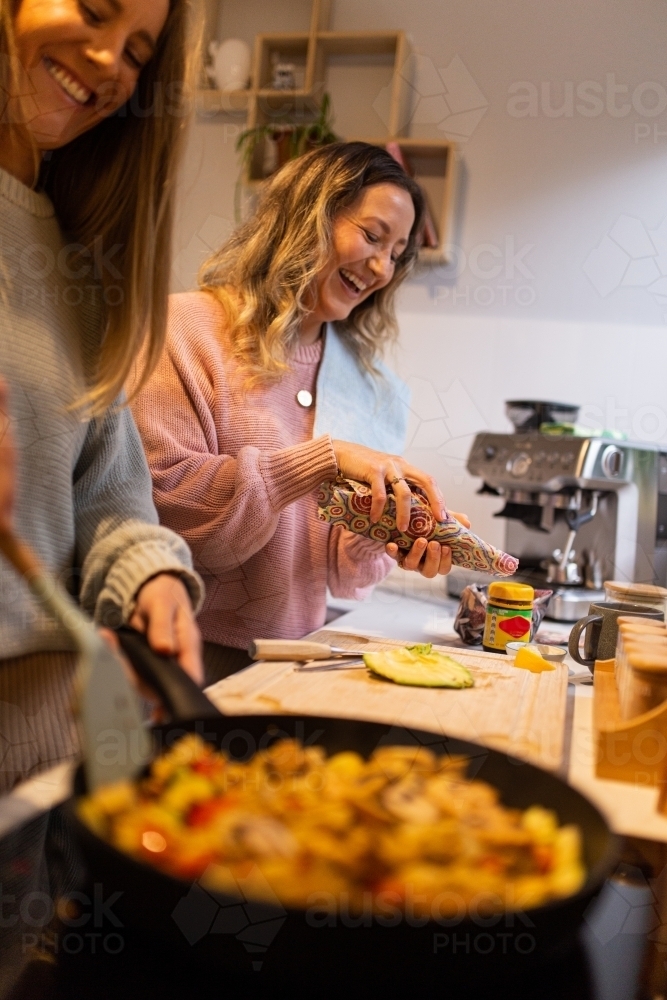 Image of Two women laughing as they cook together at home - Austockphoto