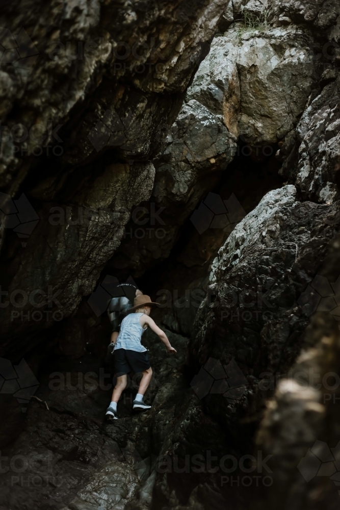 Image of Two young boys climbing rocks in cave by the beach in the ...