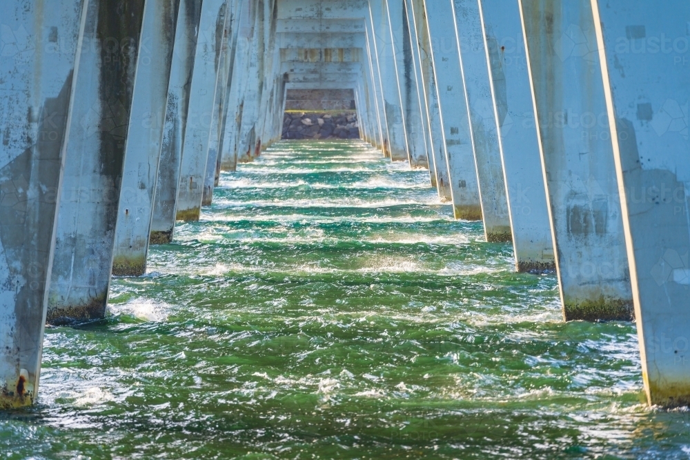 Image of View underneath a bridge of rows of angled concrete pylons and ...