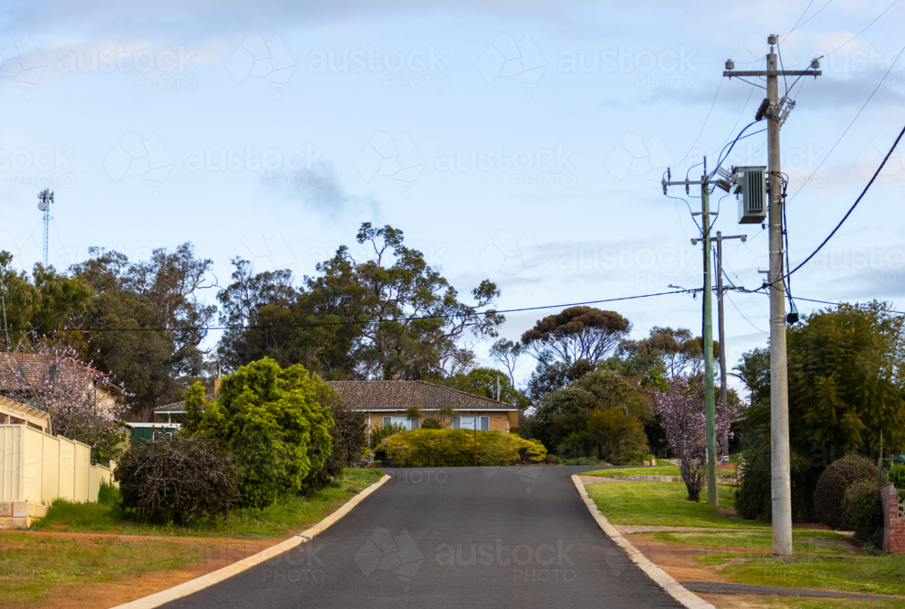 Image of view up bitumen street with power poles to a low set brick and ...