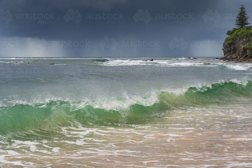 Image of Waves breaking on a beach with dark storm clouds on the ...