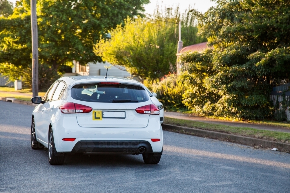 Image of White car with l plate driving on quiet suburban road ...
