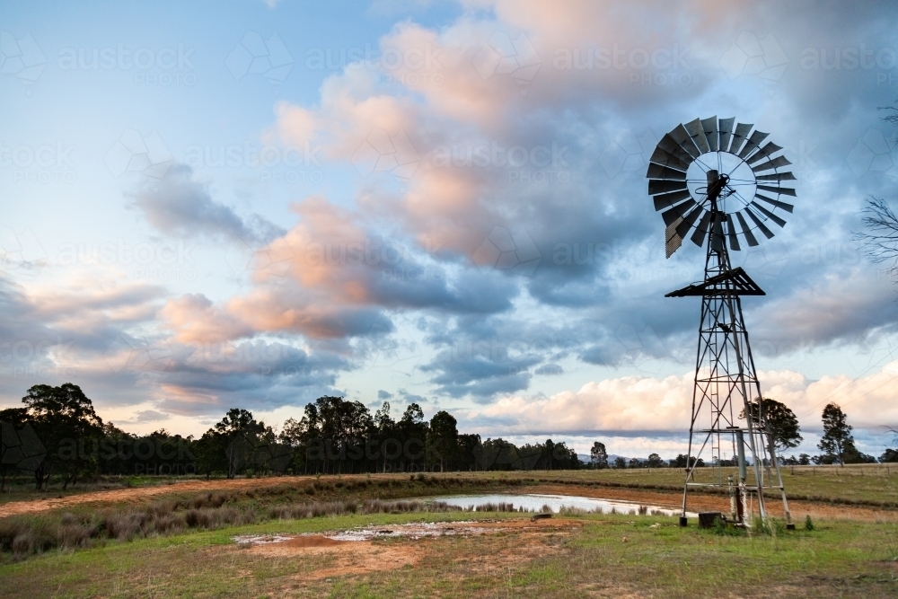 Image of Windmill beside dam on farm at sunset - Austockphoto