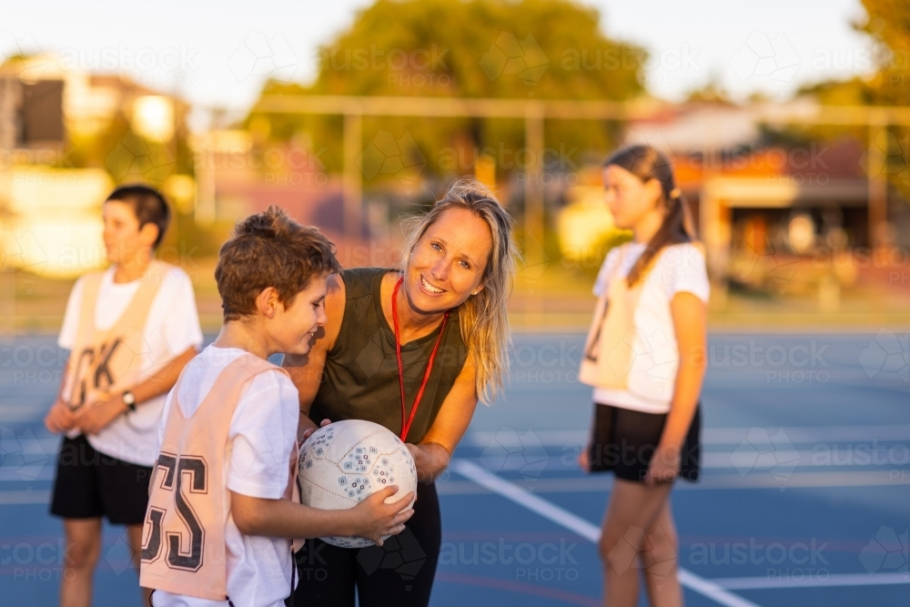 Image of woman coaching children in netball team, leaning over child ...