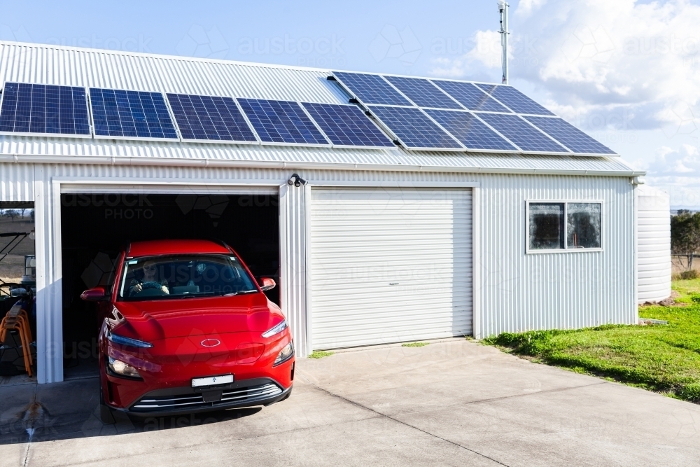 Image of Woman driving electric car out of solar powered shed on ...