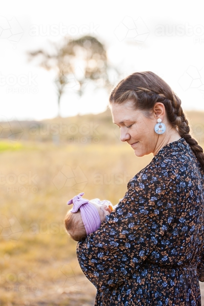 Image of Woman holding new-born baby in rural paddock - Austockphoto