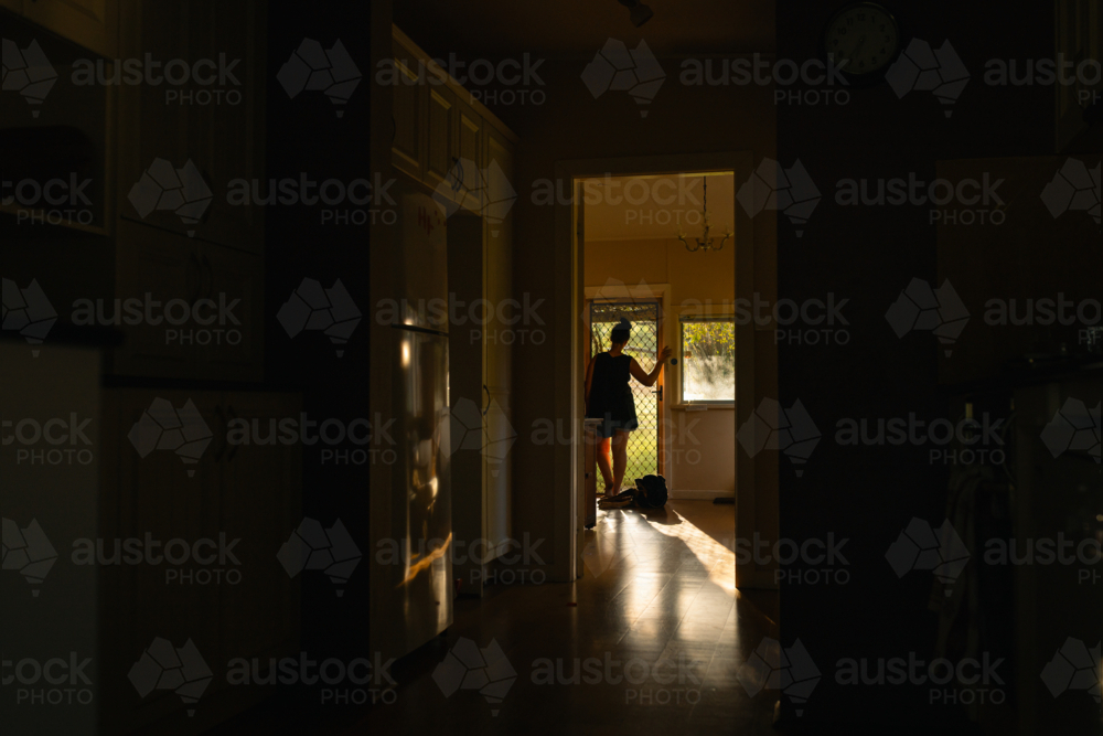 Image of Woman looking out back door of country home as afternoon ...