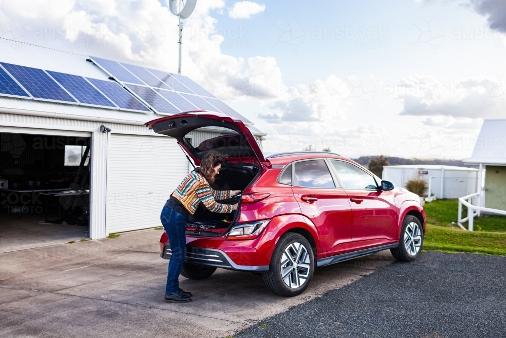 Image of woman ready to go on road trip with open boot of electric ...