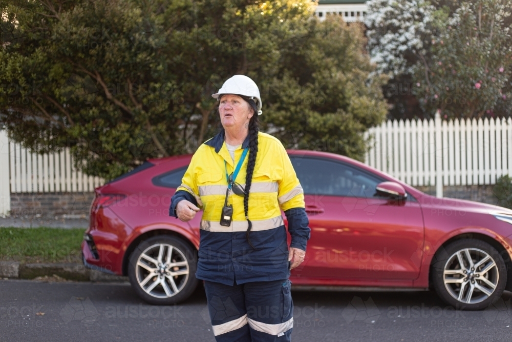 Image of Woman road worker looking away in front of a red car ...