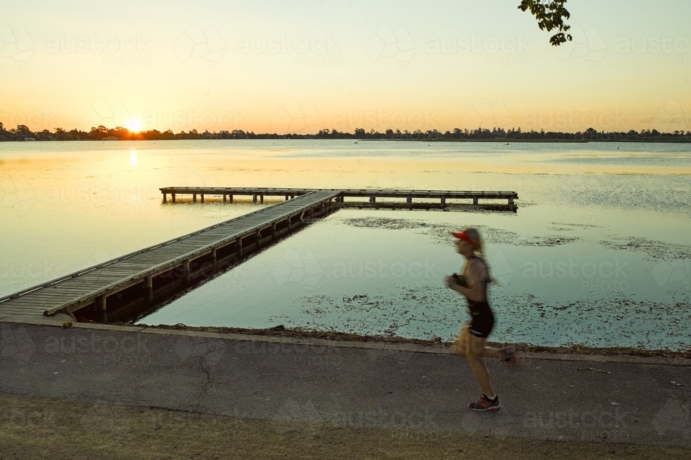 Image of Woman running around a lake at sunset - Austockphoto