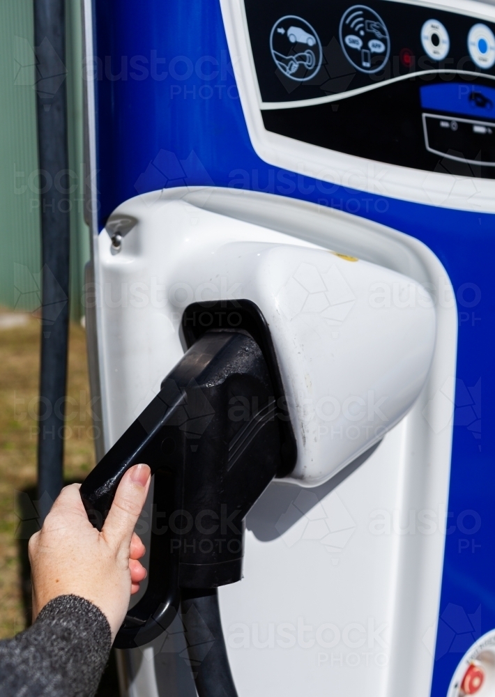 Image of Woman's hand on electric vehicle charging plug - Austockphoto