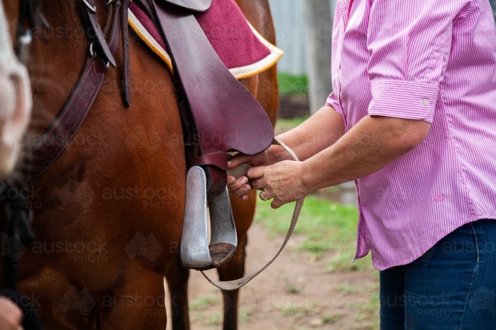 Image of Woman saddling up horse - Austockphoto