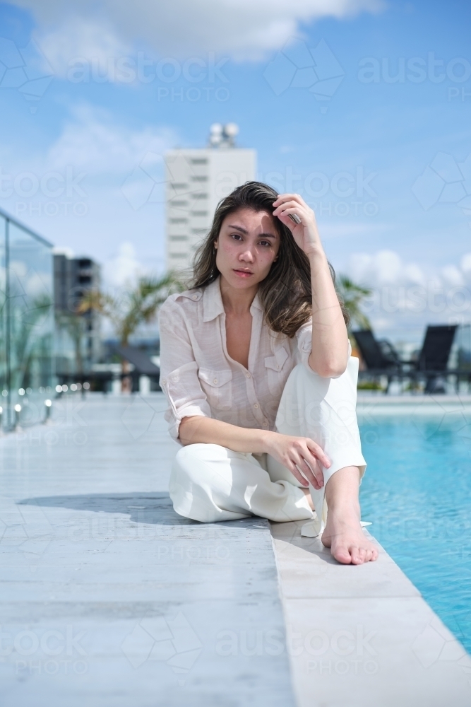 Image of Woman sitting beside rooftop pool - Austockphoto