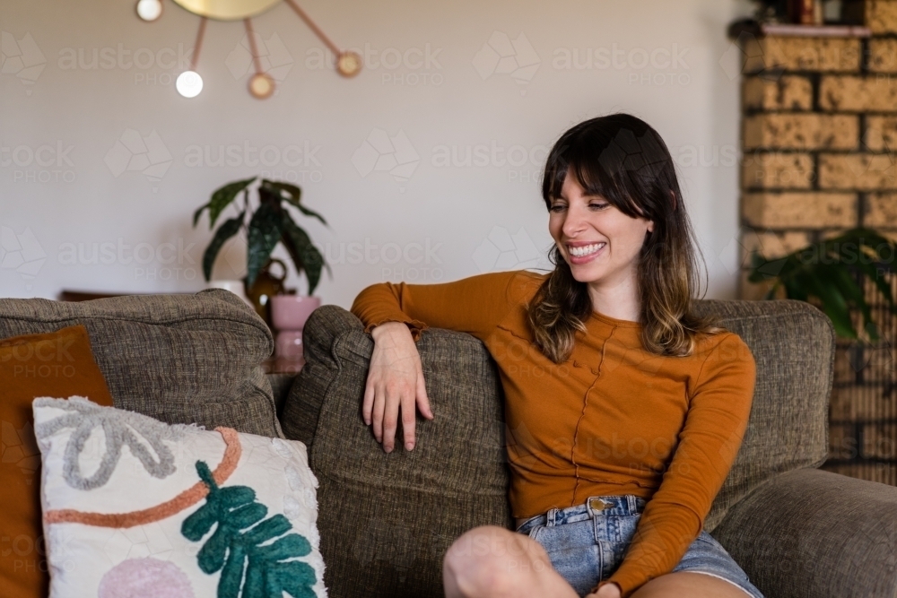 Image of woman sitting on sofa at home - Austockphoto