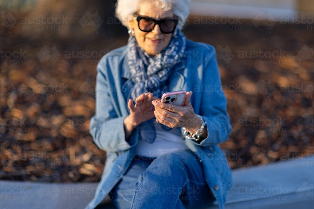 Image of woman sitting outdoors and swiping screen of smartphone with ...