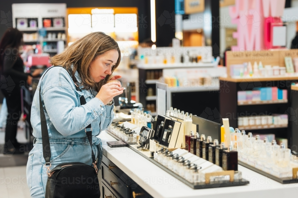 Image of Woman smelling perfume in duty free cosmetics store at the ...