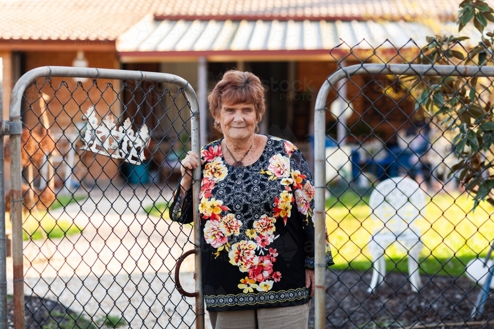 Image of woman standing in backyard holding open gate with home behind ...
