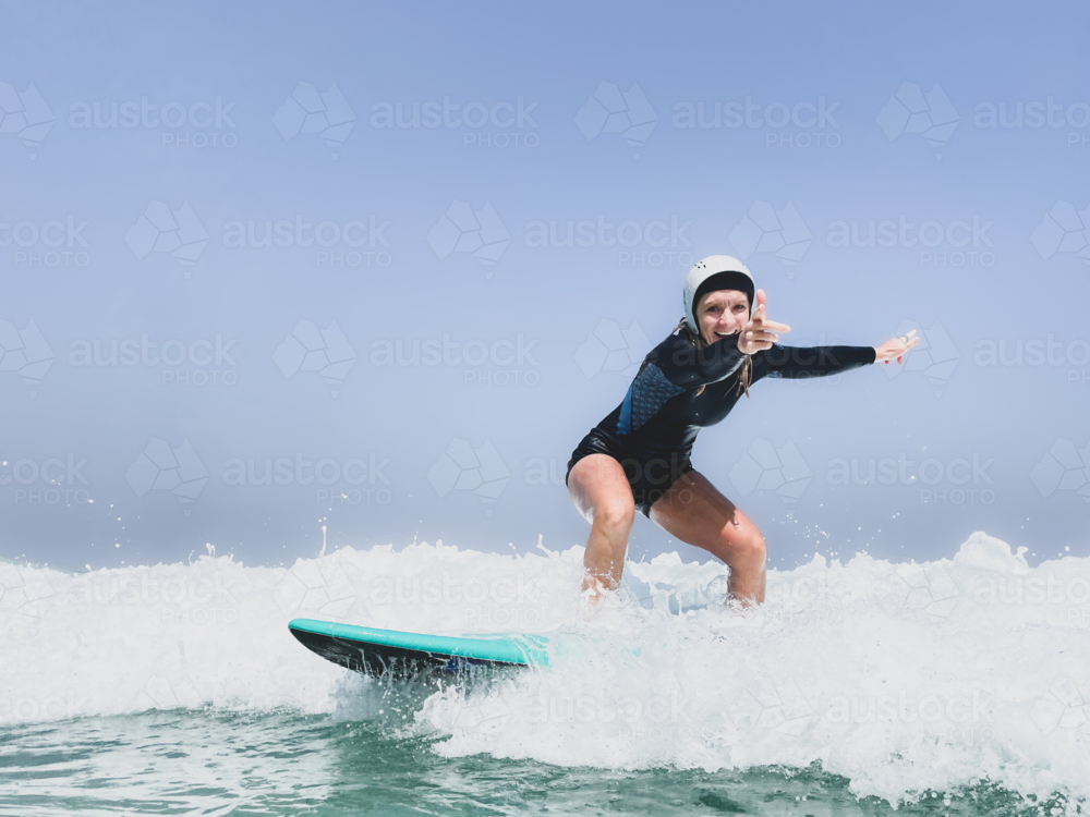 Image of Woman surfing beginner wave wearing helmet on sunny day ...