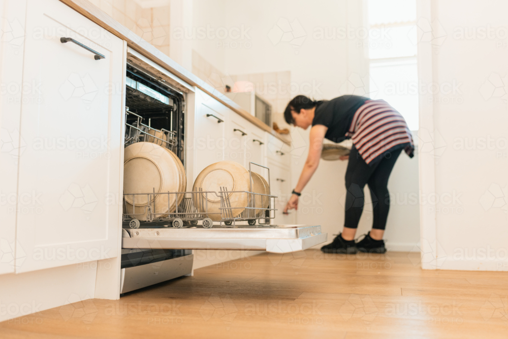 Image of Woman unloading dishwasher in bright kitchen with clean plates ...