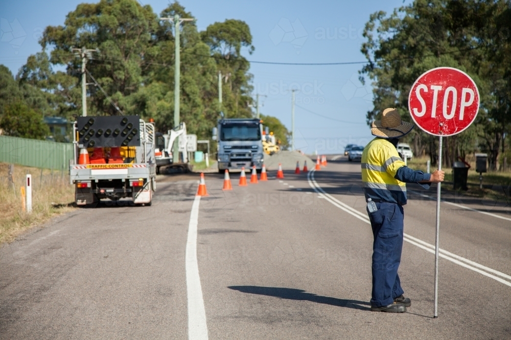 Image of Worker in hi-vis holding roadwork stop sign - Austockphoto