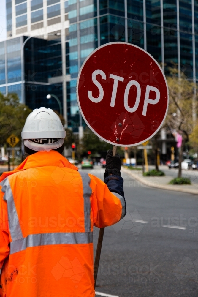 Image of worker wearing high vis holding a stop sign - Austockphoto