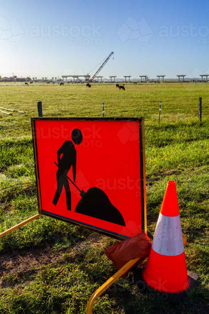 Image of Worksite warning sign beside road with farmland and crane in ...