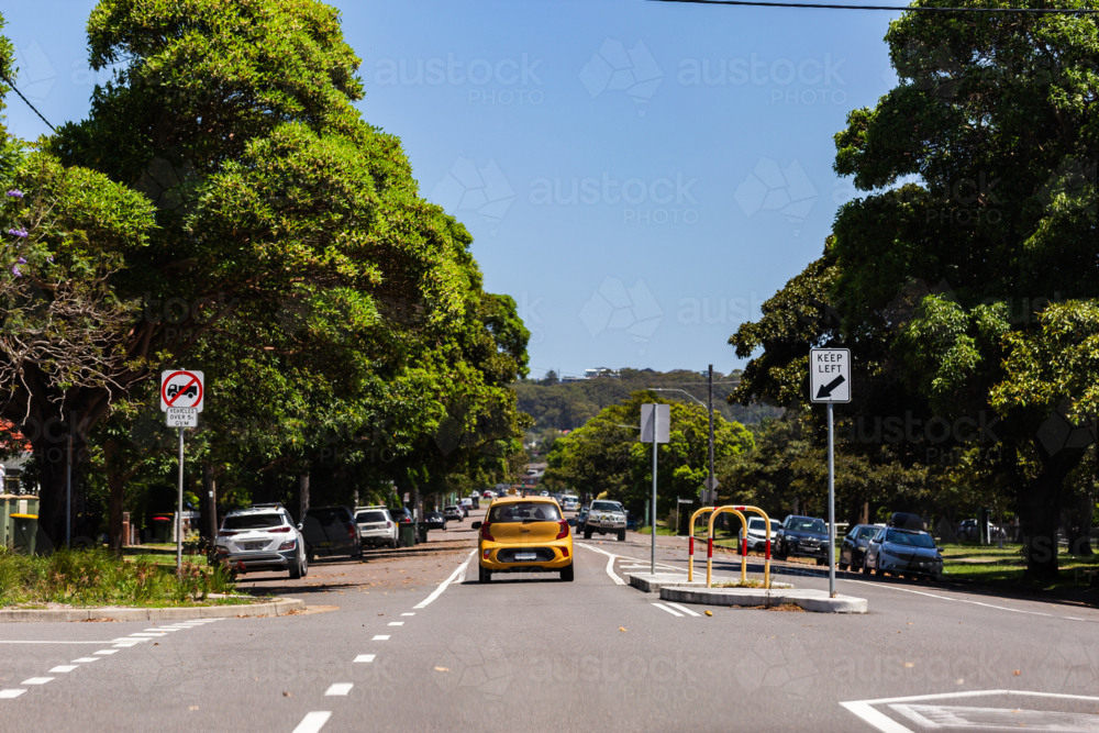 Image of Yellow car driving down road with pedestrian island and cars ...
