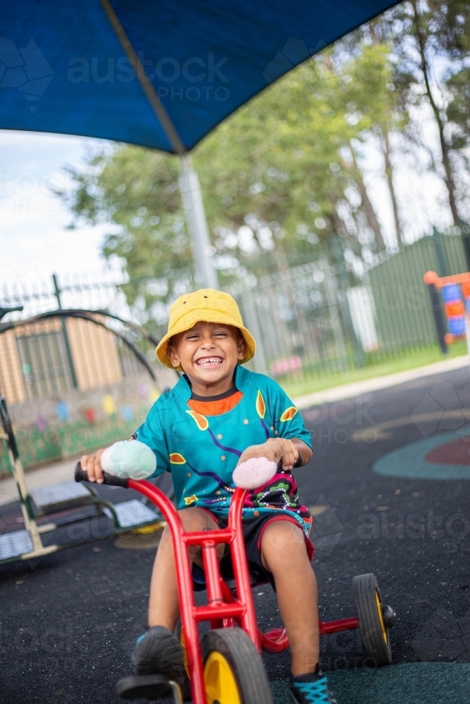 Image of Young Aboriginal boy at a preschool riding a trike and smiling ...