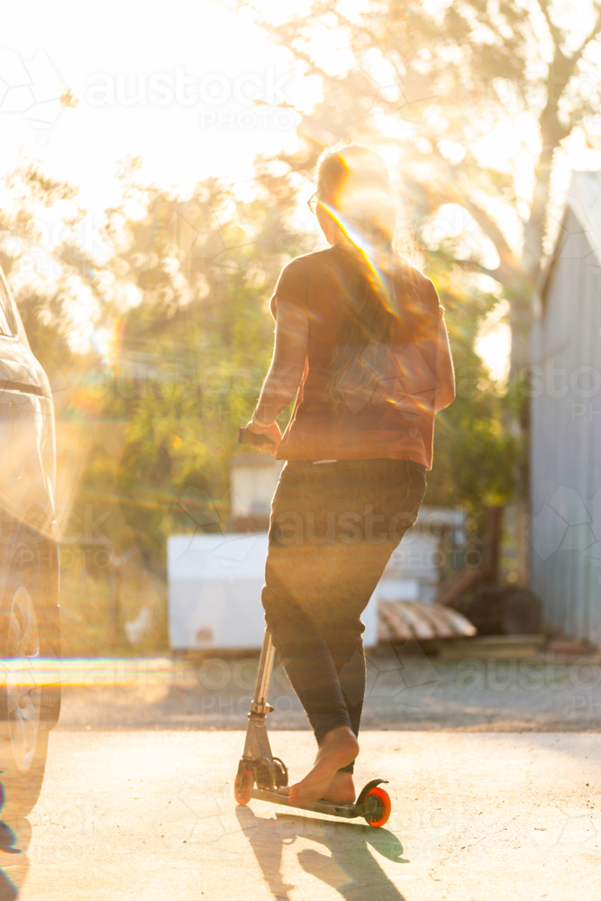 Image of Young aussie person riding barefoot on scooter in rural ...