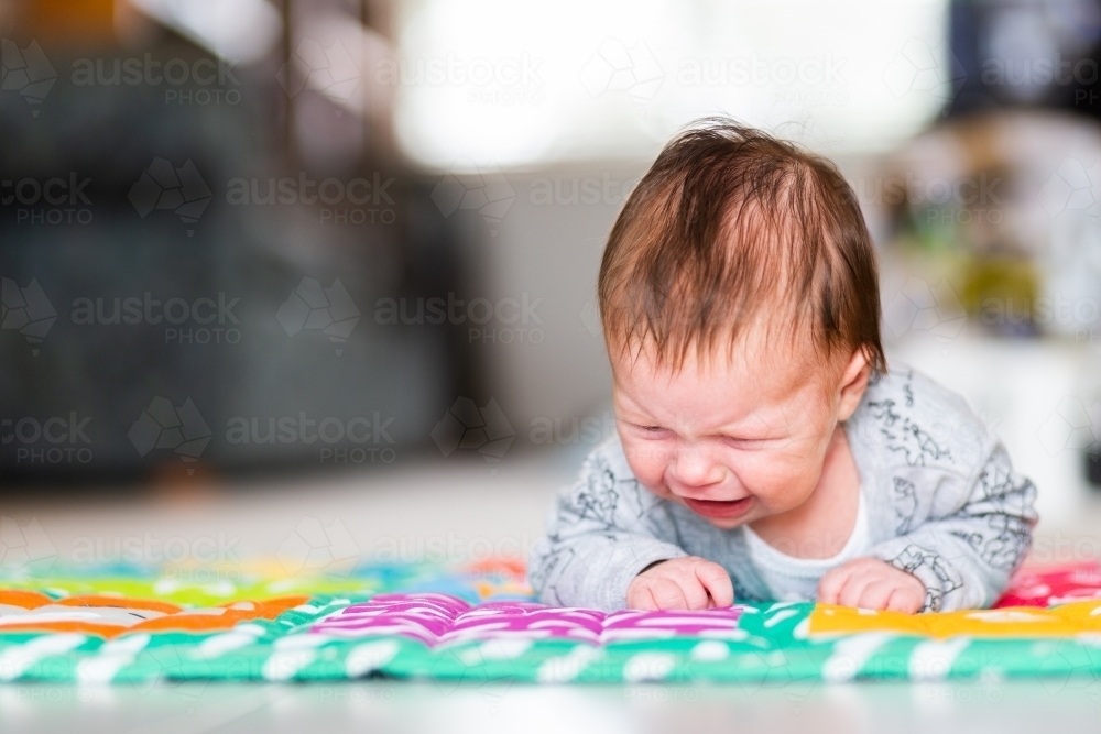 Image of Young baby doing tummy time on a mat on the floor crying ...