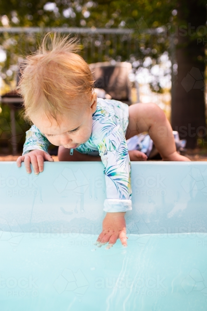 Image of Young baby leaning over edge of inground swimming pool ...