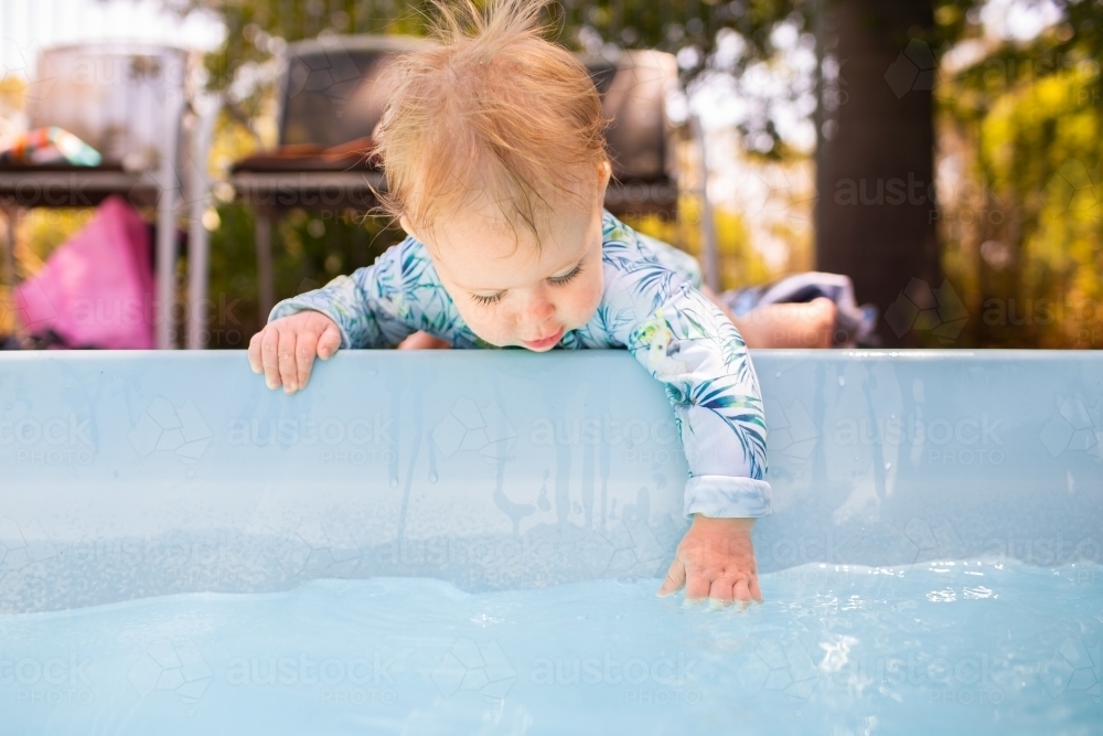 Image of Young baby leaning over edge of inground swimming pool ...