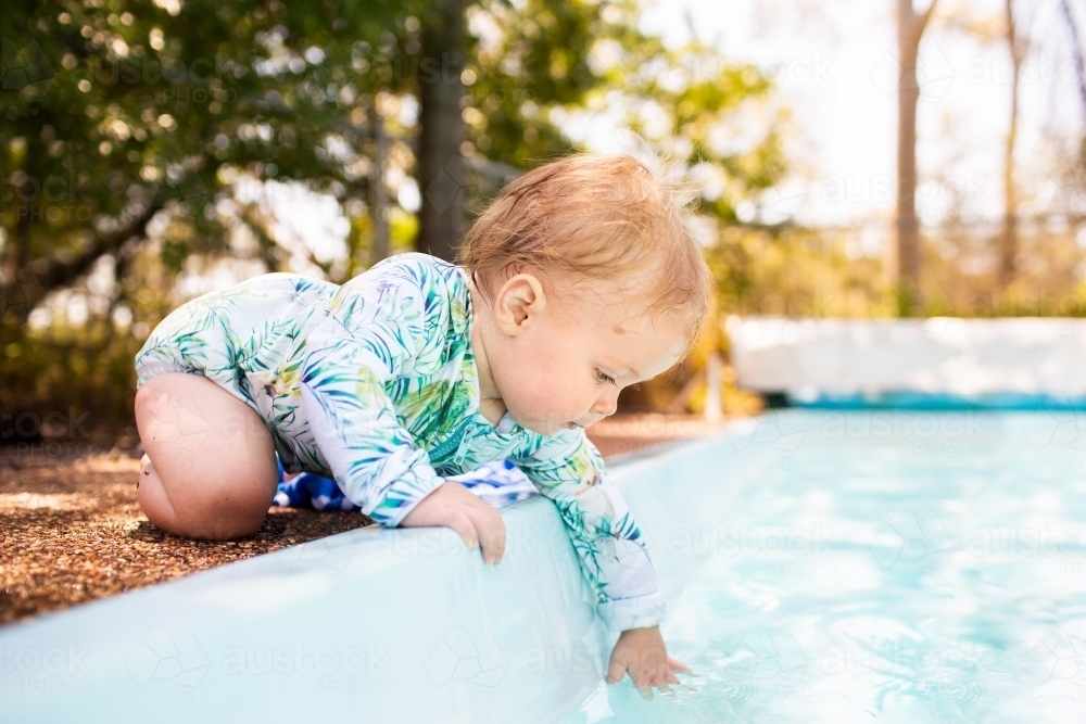 Image of Young baby leaning over edge of inground swimming pool ...