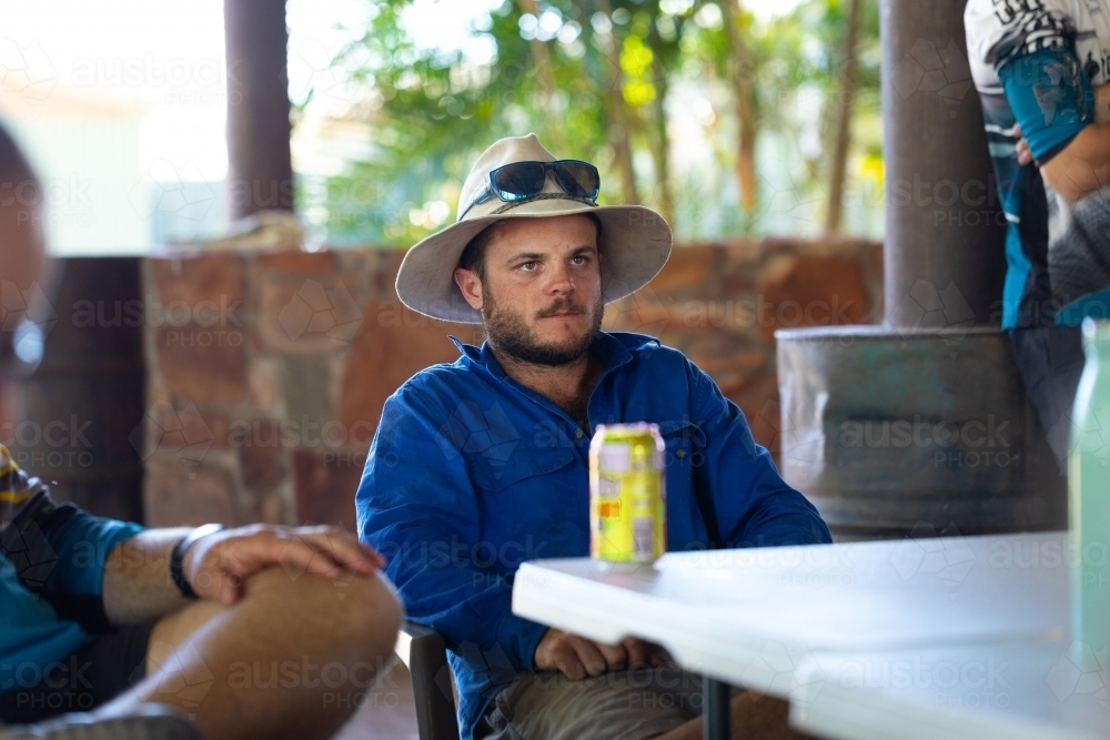 Image of young bloke sitting with mates having a beer - Austockphoto