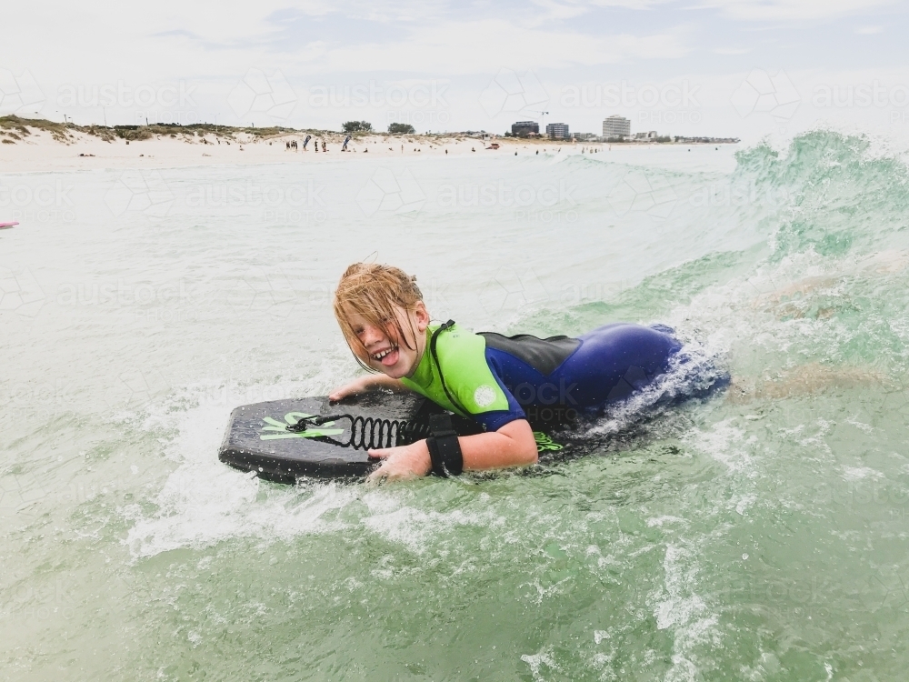 Image of Young boy boogie boarding on wave at beach - Austockphoto