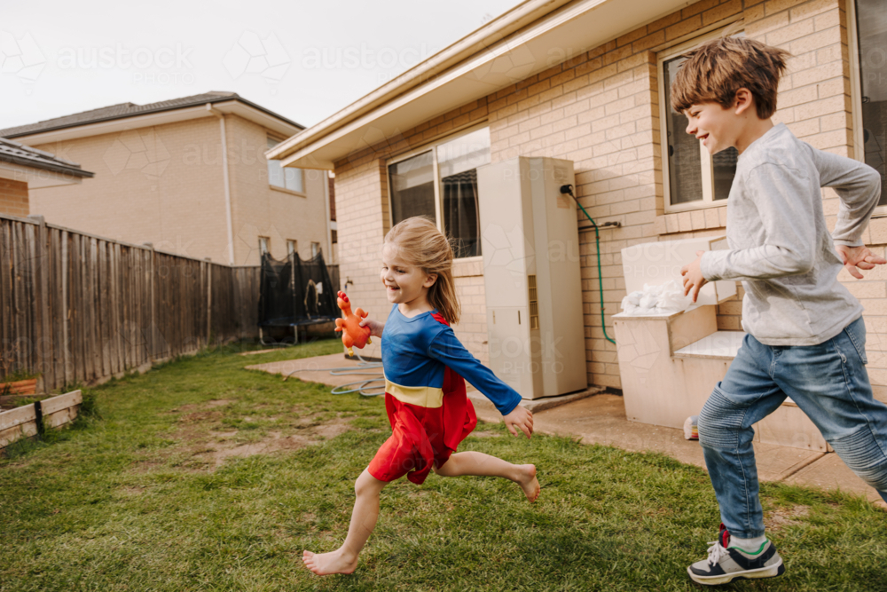 Image of Young boy chasing after the little girl in superhero costume ...