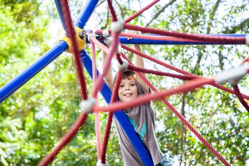 Image of Young boy climbing spiderweb playground equipment at park ...