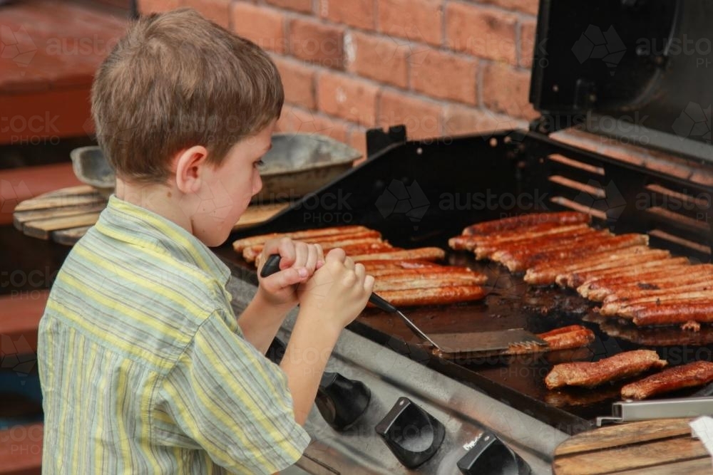 Image of Young boy cooking sausages on the barbecue - Austockphoto