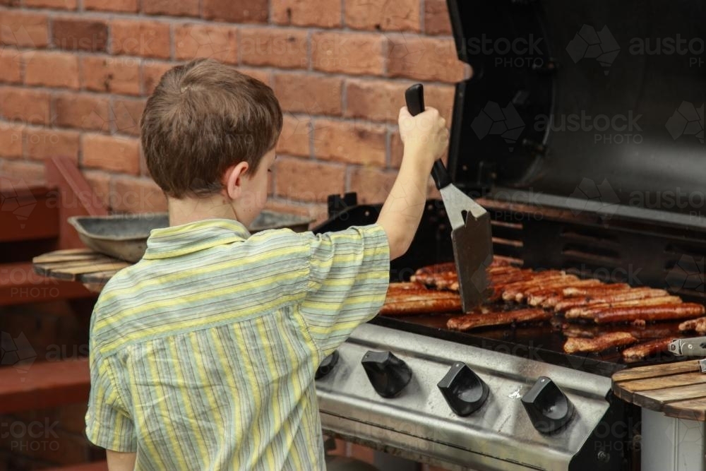 Image of Young boy cooking sausages on the barbecue - Austockphoto