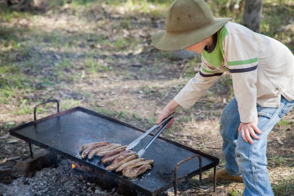 Image of Young boy helping cook snags on the hot plate - Austockphoto